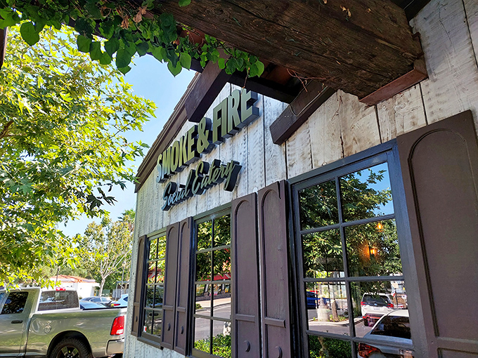 The weathered wood exterior of Smoke And Fire beckons like a rustic oasis in Riverside, promising smoky treasures behind that bright red door.
