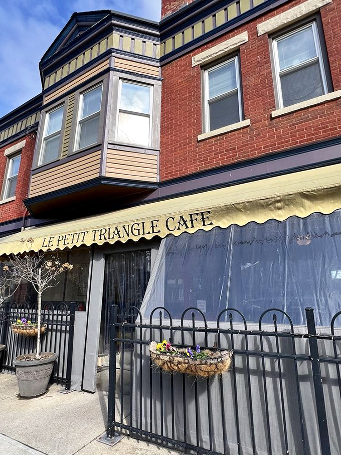The charming brick facade of Le Petit Triangle Cafe beckons with its distinctive yellow awning and wrought-iron fence—a little slice of Paris on a Cleveland corner.