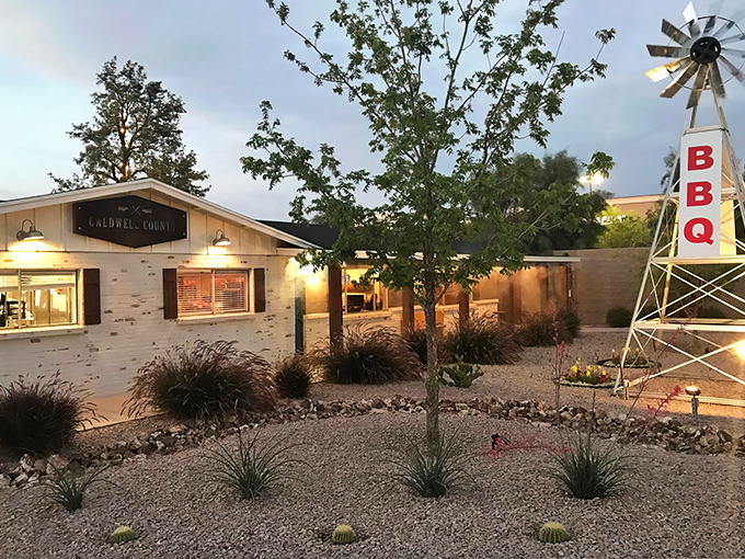 The Texas-style windmill stands sentinel outside Caldwell County BBQ, a desert oasis where smoke signals promise delicious things to come.