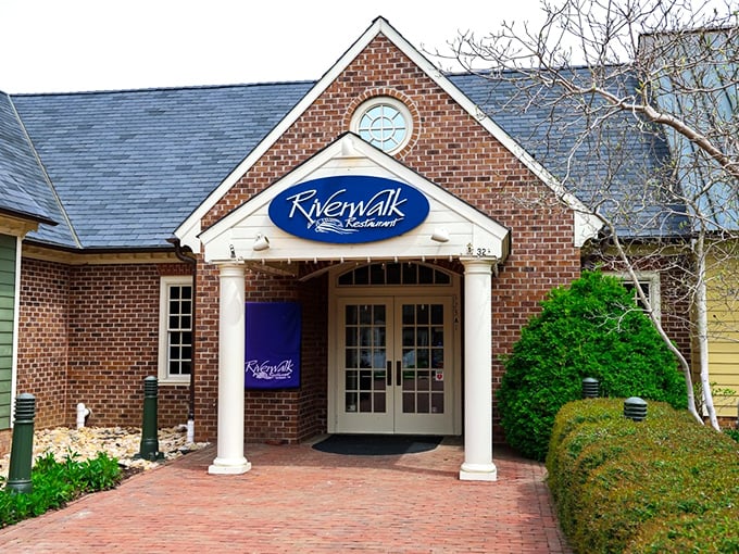 The welcoming brick façade of Riverwalk Restaurant stands like a culinary lighthouse, beckoning hungry travelers with its classic colonial charm and blue signage.