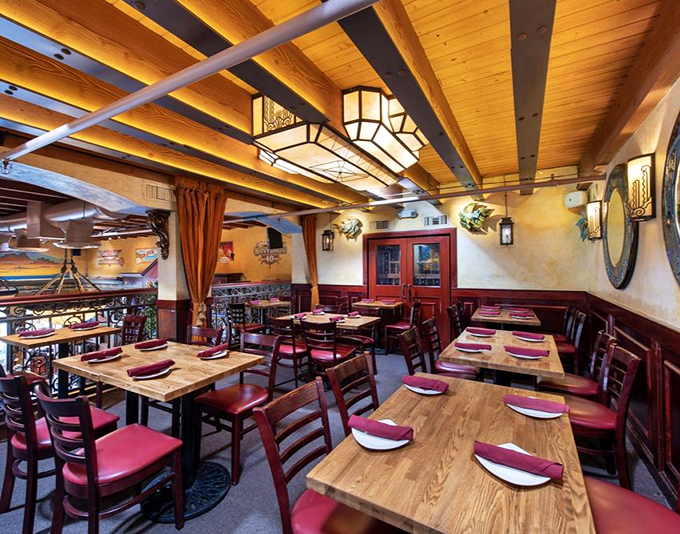 Warm wood beams, lantern lighting, and burgundy accents create a dining room that feels like the world's coziest ship's cabin – minus the seasickness.