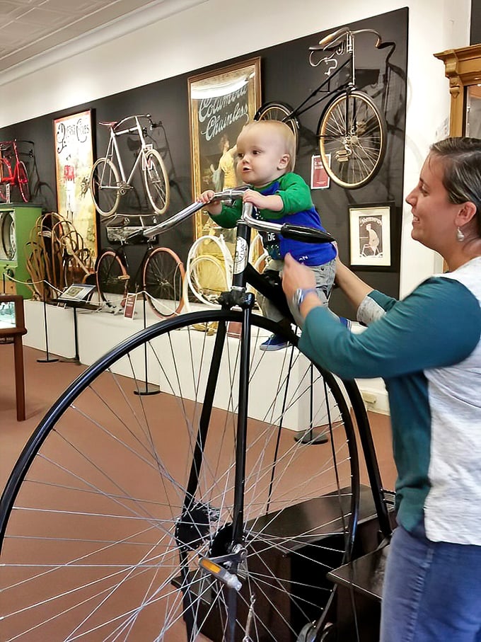 A young cycling enthusiast gets acquainted with a penny-farthing. Starting them early on vintage bikes—training wheels not included for historical accuracy.