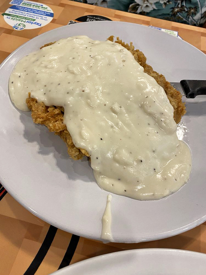Chicken fried steak swimming in peppery cream gravy—a Texas breakfast tradition that answers the question: "How do I need enough energy to last until dinner?"