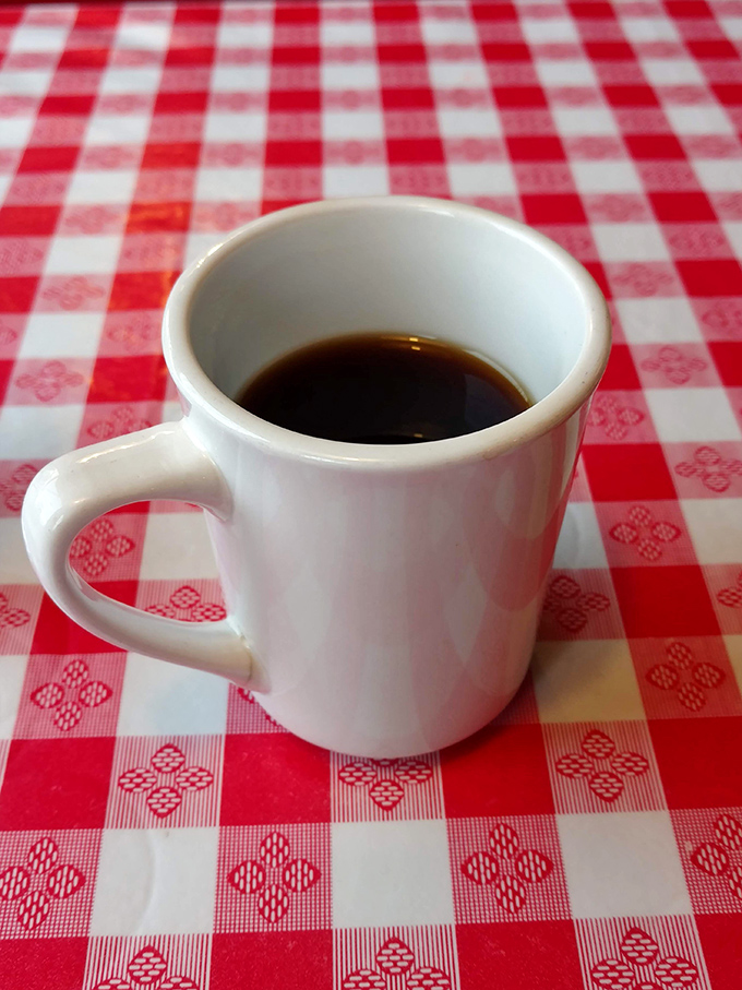The humble white mug on checkered tablecloth – where coffee isn't just a beverage, but the lifeblood of diner culture and morning conversations.