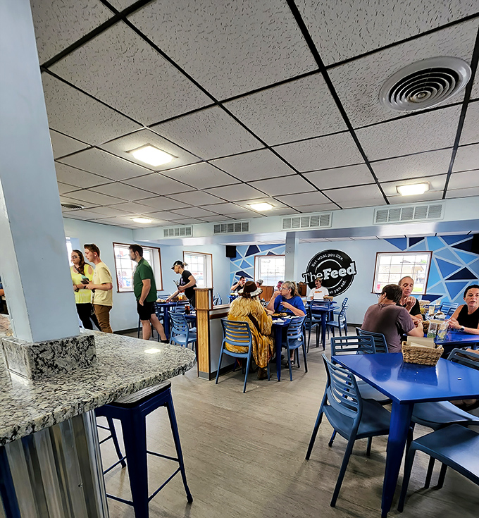 A bustling dining room where strangers become neighbors over great food. The blue chairs aren't just furniture—they're invitations.