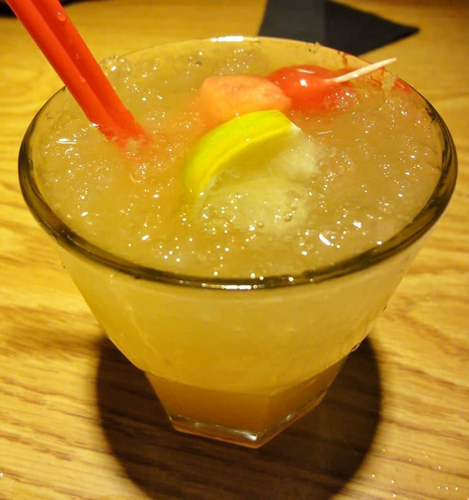 The legendary Mai Tai arrives like liquid vacation – a fishbowl of tropical promise garnished with enough fruit to count as nutrition.
