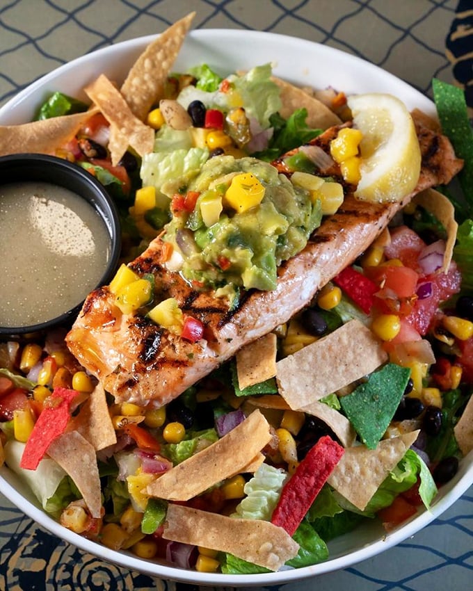 A salad that doesn't apologize for being healthy – grilled salmon and colorful tortilla strips creating a fiesta on your plate.