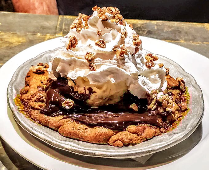 Dessert architecture at its finest – a warm cookie foundation supporting melting ice cream, whipped cream, and candied pecans in perfect structural harmony.