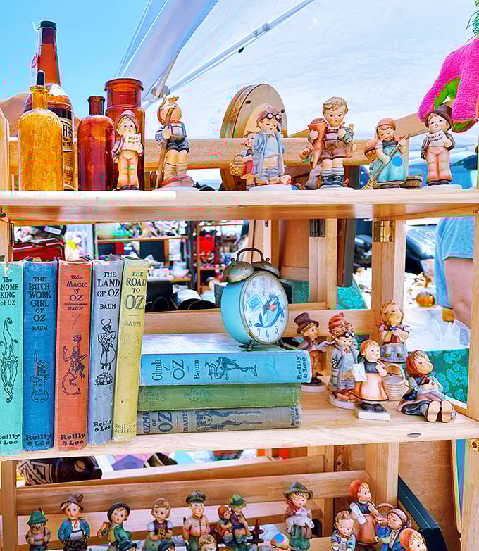 A nostalgic lineup of vintage Hummel-style figurines stands at attention beside colorful Wizard of Oz books—childhood memories for sale, no batteries required.