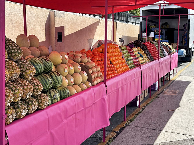 Fruit architecture at its finest – melons, pineapples, and oranges stacked with geometric precision under a celebratory pink canopy.