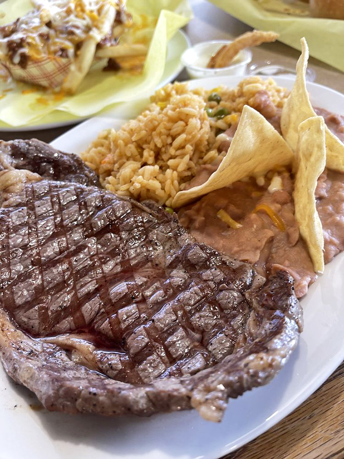 A perfectly grilled steak alongside Spanish rice and refried beans—the kind of plate that makes you want to tip your hat to the grill master.