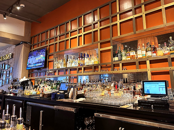 A bar backed by vibrant orange that showcases bottles like trophies—liquid amber treasures waiting to transform your evening. 