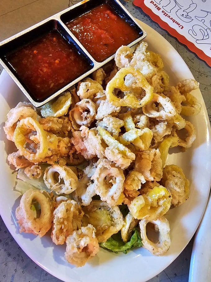 A mountain of golden-fried calamari rings with two dipping sauces standing at attention. Crispy, tender seafood that disappears from the plate faster than you can say "more, please."