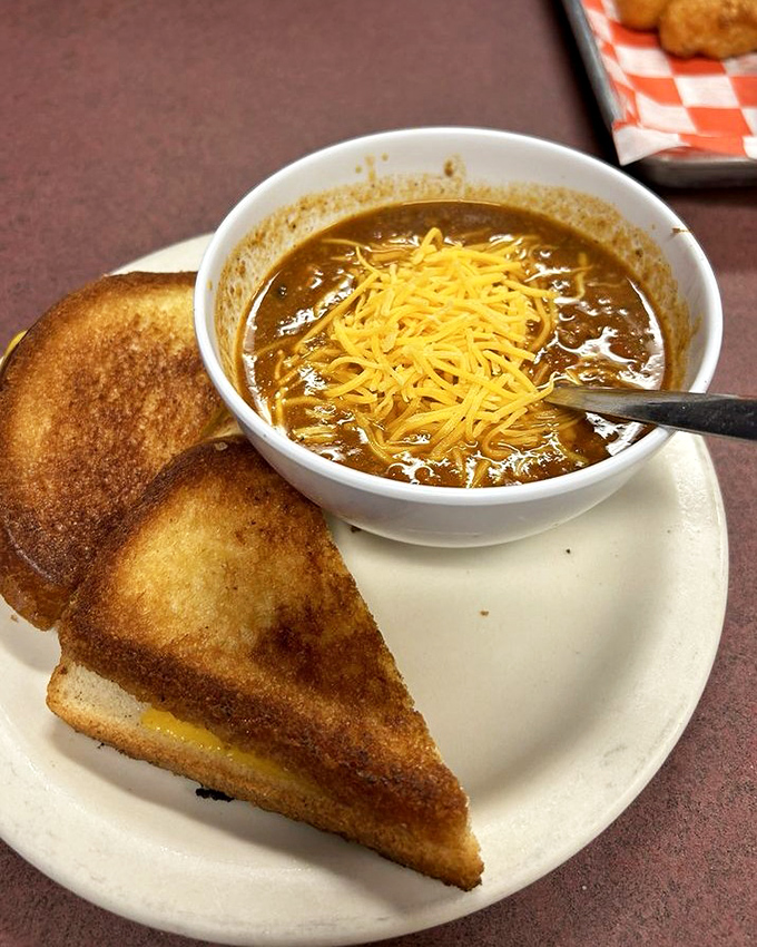 A bowl of homemade chili topped with melted cheese alongside a perfectly grilled cheese sandwich—comfort food's greatest power couple. 
