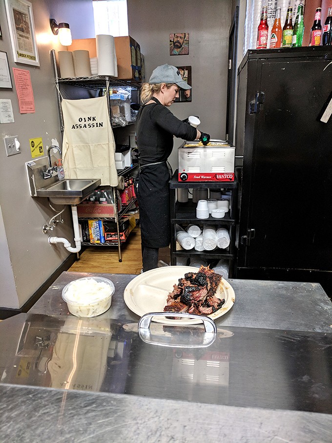 Behind the scenes magic where smoke meets meat—note the "Oink Assassin" apron, a job title that should definitely appear on business cards.