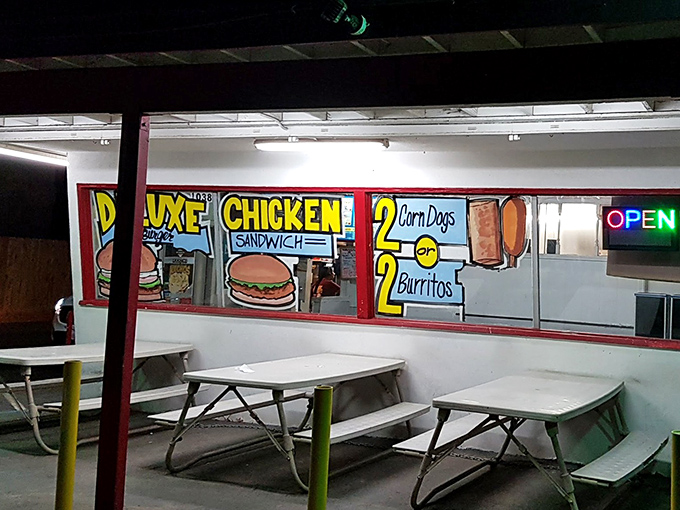 Outdoor seating with hand-painted window art advertising deluxe chicken sandwiches and corn dogs—simple pleasures in the California sun.