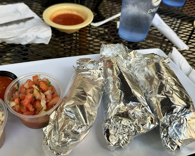 Foil-wrapped treasures flanked by fresh pico de gallo—the silver packages aren't just tacos; they're gifts your taste buds have been patiently waiting to unwrap.