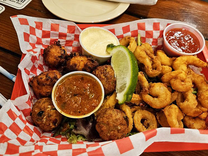 The seafood sampler that settles all arguments—fritters, calamari, and shrimp sharing a basket in perfect harmony with dipping sauces playing referee.