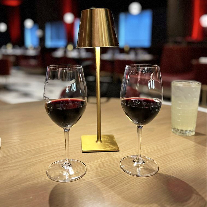 Two glasses of ruby-red wine flanking a gold table lamp—because at Fahrenheit, even your drinks get mood lighting.