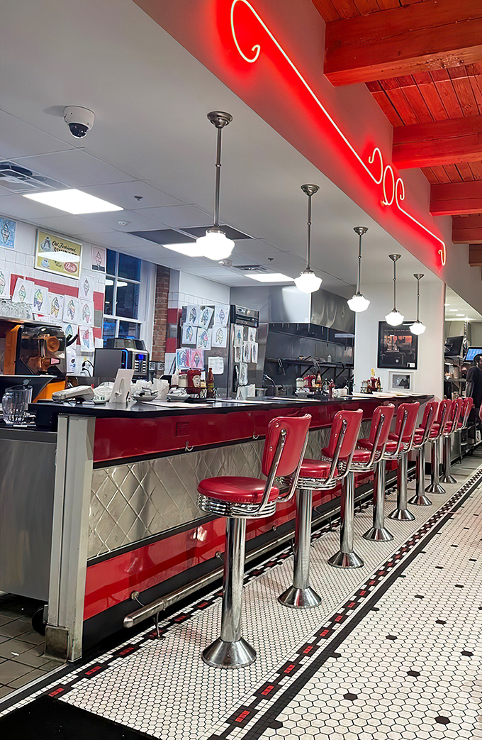 The counter where magic happens—gleaming red stools invite you to sit and watch soda jerks orchestrate sweet symphonies beneath neon glow.