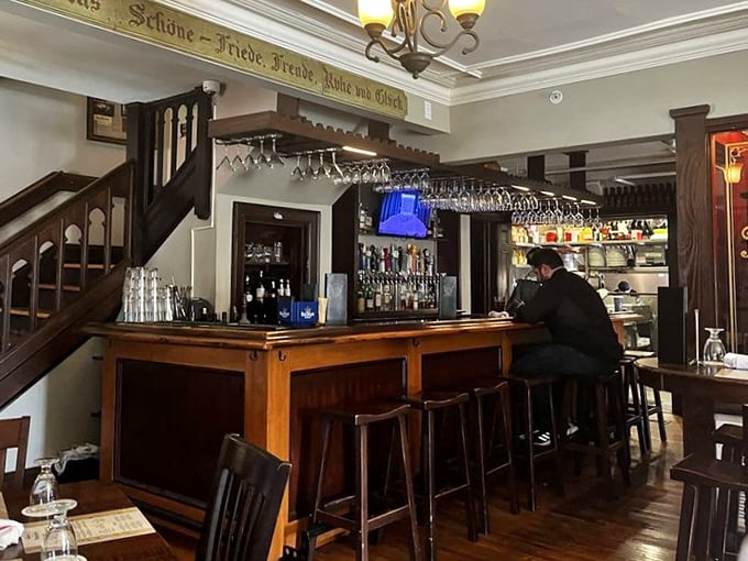 The bar area features hanging glassware and German inscriptions above—a place where "Prost!" replaces "Cheers!" and beer is treated with proper reverence.