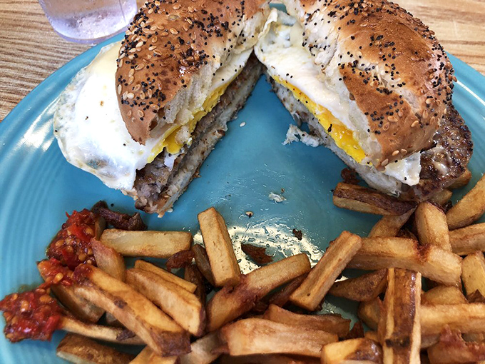 The breakfast sandwich cut in half reveals its secrets—a perfectly cooked egg and savory meat nestled between a toasted everything bagel. 