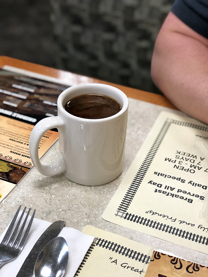 The humble coffee mug—unassuming vessel of morning salvation, sitting patiently beside silverware wrapped with the care of a grandmother's hug.