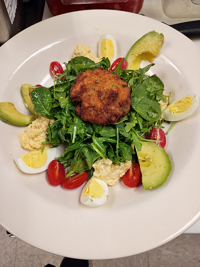 This crab cake sits atop greens like a golden crown, surrounded by colorful vegetables fit for royalty.