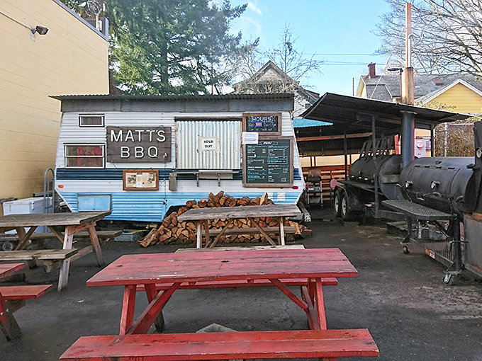 The humble blue trailer with its wooden sign promises more flavor than most fancy restaurants. Those stacked logs aren't decoration – they're flavor in waiting.