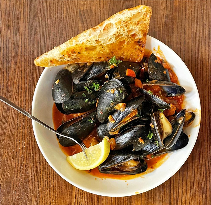These mussels aren't just swimming in sauce—they're luxuriating in it. Served with grilled bread for sopping up every last drop of that glorious broth.