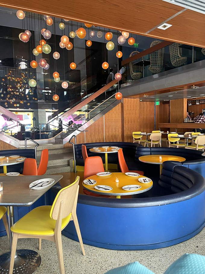 Yellow tables pop against blue banquettes in a color scheme that feels both retro and timeless, like a '60s movie set reimagined for today.