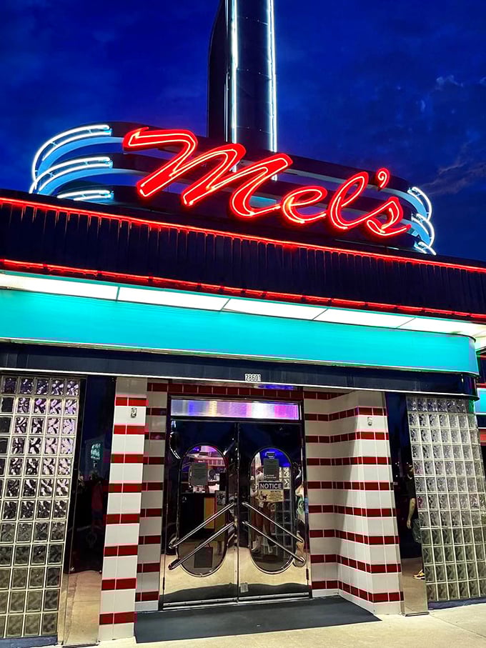 The neon "Mel's" sign glows like a lighthouse for the hungry, guiding travelers to a safe harbor of burgers and shakes.