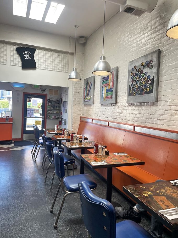 White brick walls showcase vibrant art while orange booths invite you to slide in and stay awhile. Diner design that feeds the soul before food arrives.