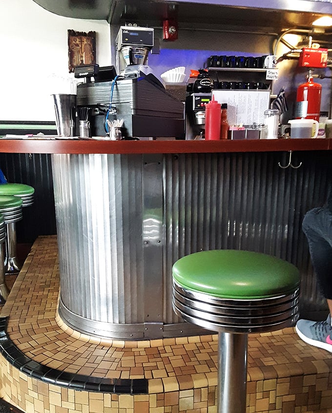 That corrugated metal counter with mint green stools—the breakfast bar where strangers become neighbors over coffee refills and shared weather complaints.
