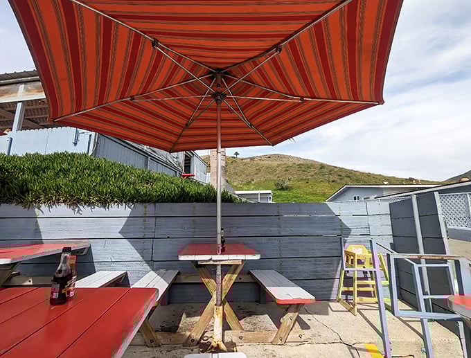 Striped umbrellas and red picnic tables create an inviting outdoor dining space steps from paradise.