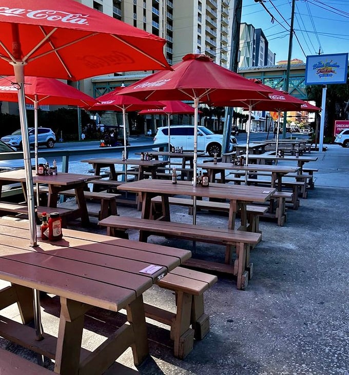 Red umbrellas shade wooden picnic tables outside Shuckums, creating the perfect spot for enjoying seafood with a side of people-watching.