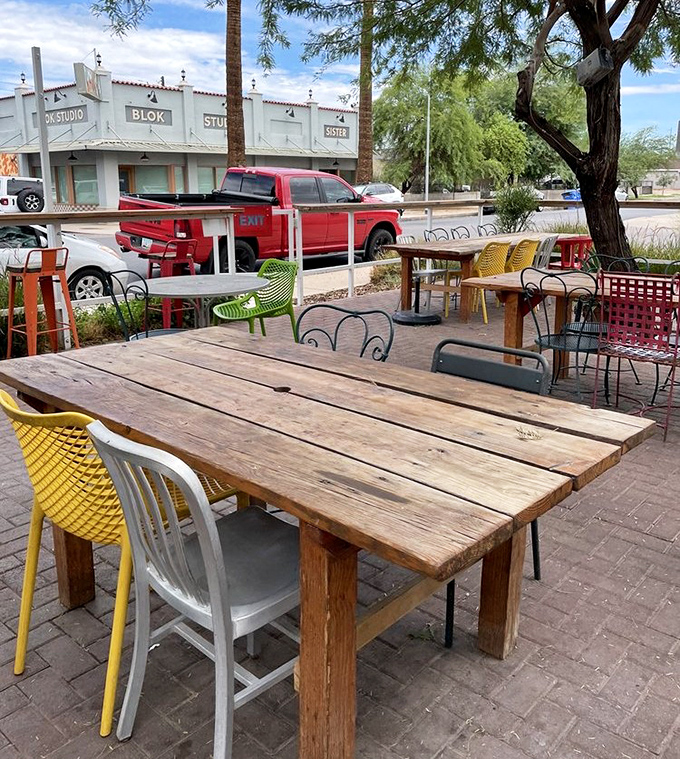 Mismatched chairs in cheerful colors surround rustic wooden tables – outdoor dining with the casual charm of your coolest friend's backyard party.