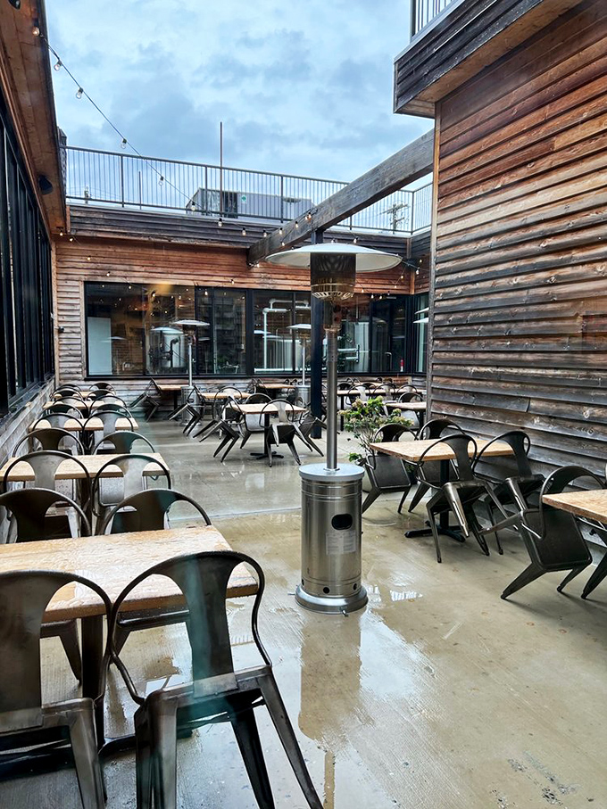Rain-slicked wooden decking and industrial metal chairs create an urban oasis where string lights will soon cast their magic over evening conversations and craft brews.
