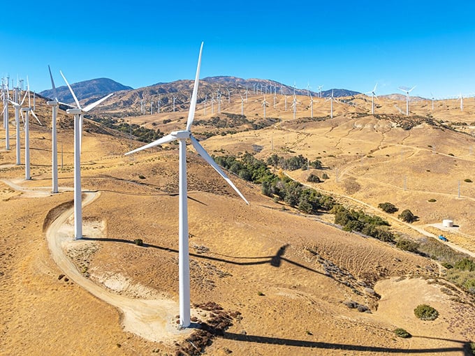 Wind turbines dot the landscape like modern art installations, silently harvesting mountain breezes while cows graze below, unbothered by progress.