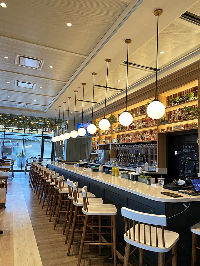 The bar stretches like a runway, with pendant lights marching in formation above. It's not just a place to drink—it's theater for the cocktail arts.
