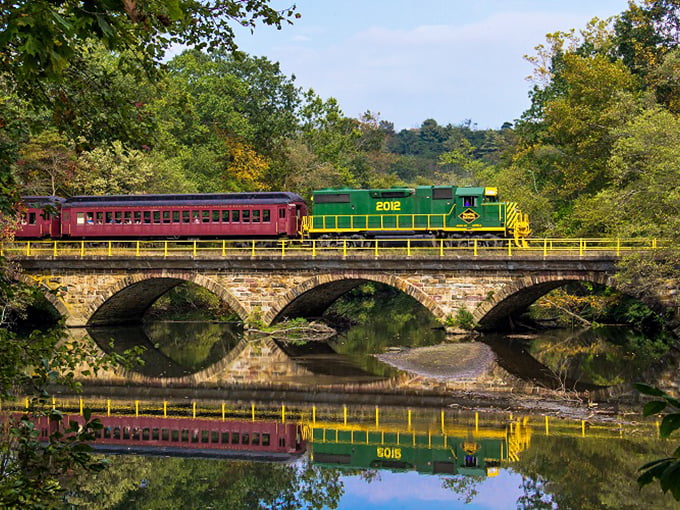 This stone arch bridge doesn't just span water—it connects centuries, carrying colorful train cars over reflections that double the visual feast.