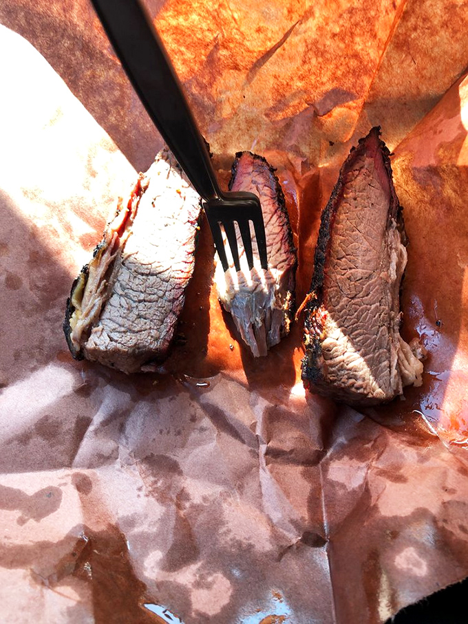 Brisket sliced against the grain revealing that telltale pink smoke ring—the barbecue equivalent of a diamond necklace. Meat jewelry at its finest.