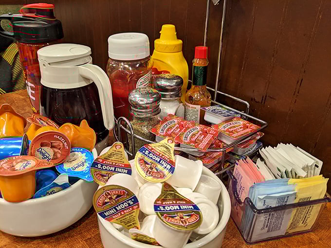 The condiment caddy—that miniature United Nations of flavor enhancement where ketchup diplomacy and sugar packet politics play out daily.