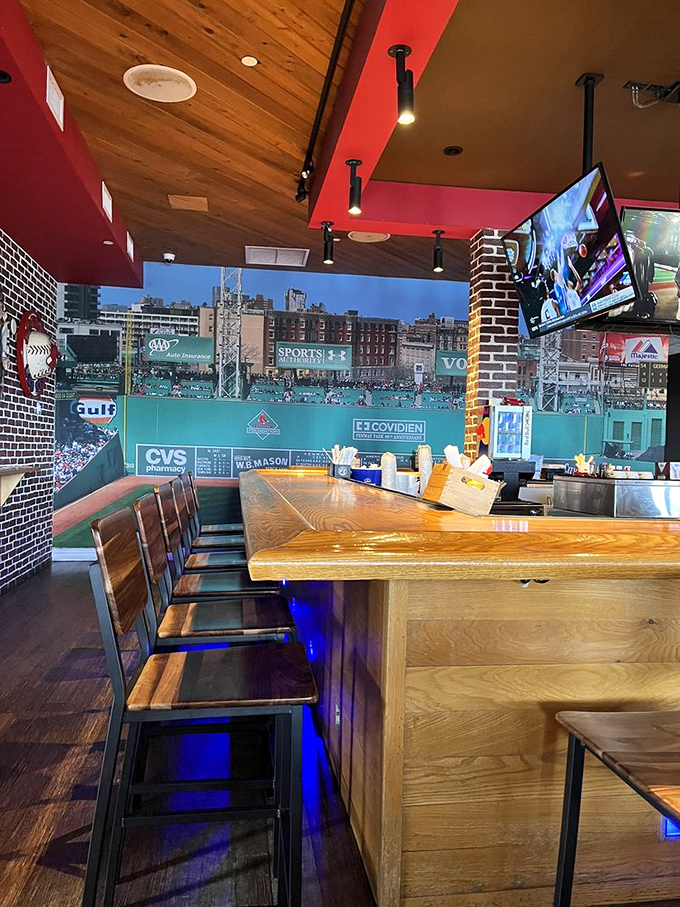 Where Boston meets beach: wooden bar seating facing Fenway's Green Monster mural. Baseball and beachfront—an unlikely marriage that somehow works perfectly.