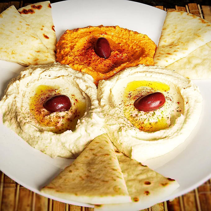 Hummus trio with kalamata olives standing guard—creamy, dreamy chickpea perfection that makes store-bought versions hide in shame.