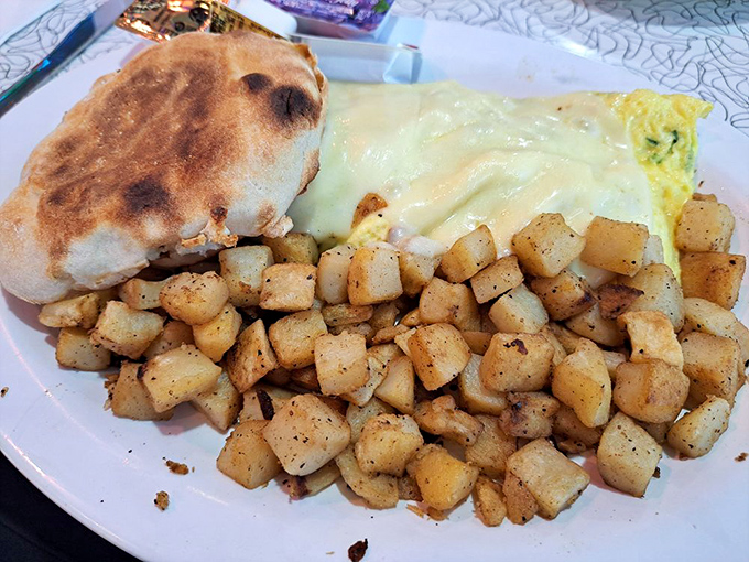 Breakfast architecture at its finest. Perfectly seasoned home fries, English muffin, and an omelet draped in melted cheese—pure morning magic.