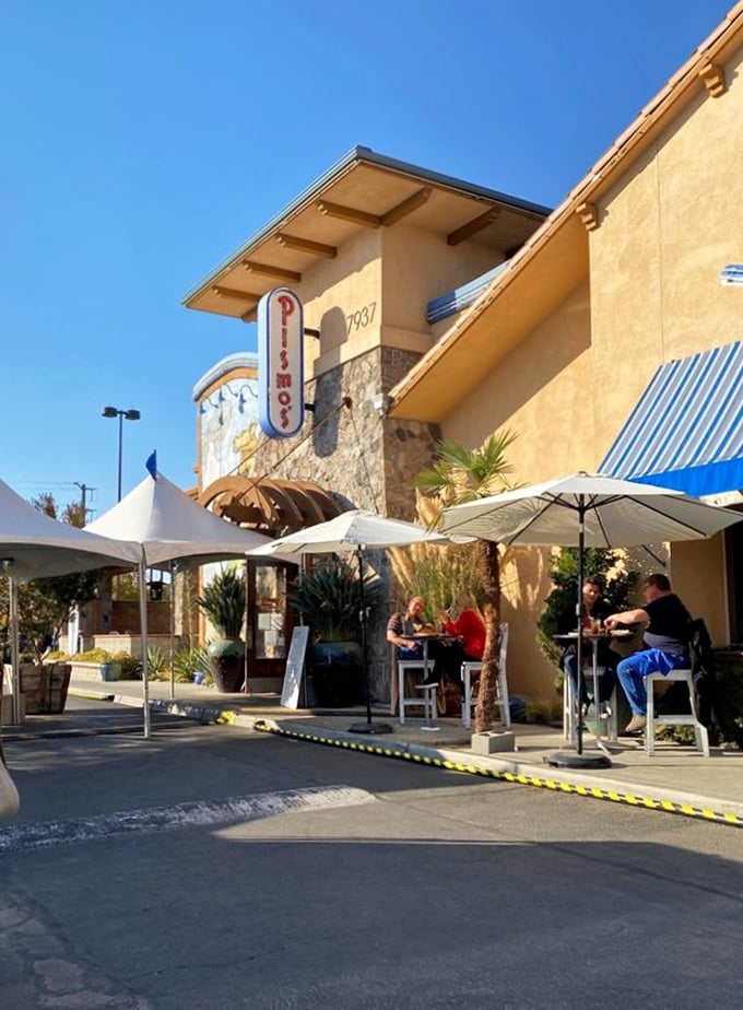 Outdoor tables under white umbrellas create impromptu coastal dining, even in Fresno's heat. The palm-fringed façade completes the coastal illusion.