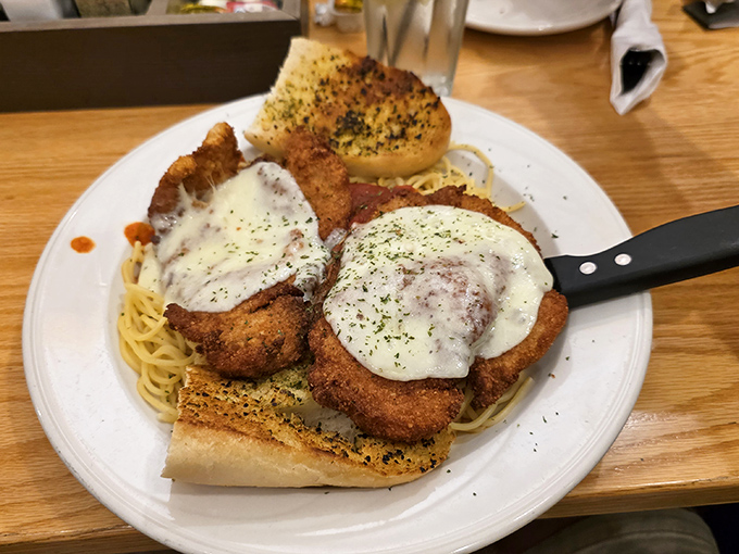 Chicken parmesan that doesn't just sit on pasta—it rules over it with crispy, cheesy authority and garlic bread courtiers.