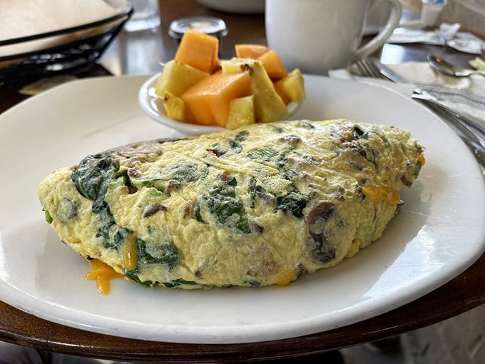 This omelet doesn't just contain vegetables—it celebrates them, wrapped in a perfectly executed egg blanket alongside fresh fruit.