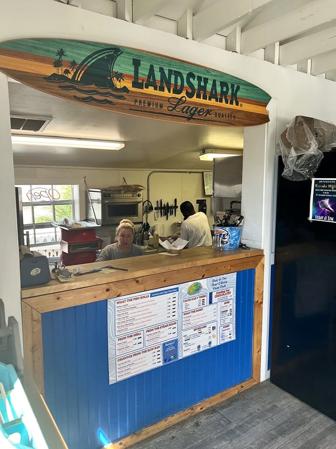The kitchen window: where seafood magic happens under the watchful eye of a Landshark surfboard guardian.